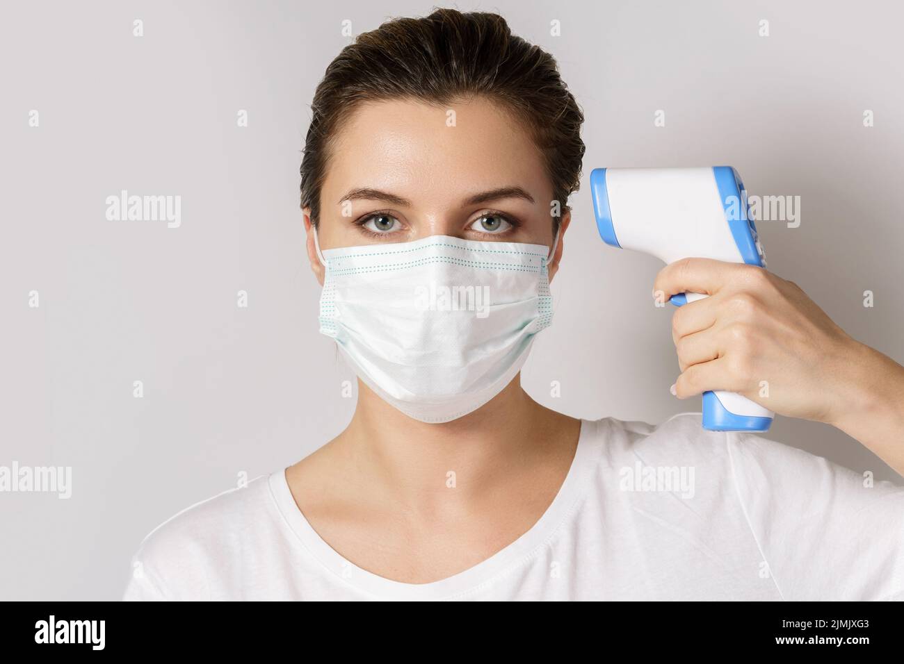 Young woman wearing face mask is measuring body temperature Stock Photo ...