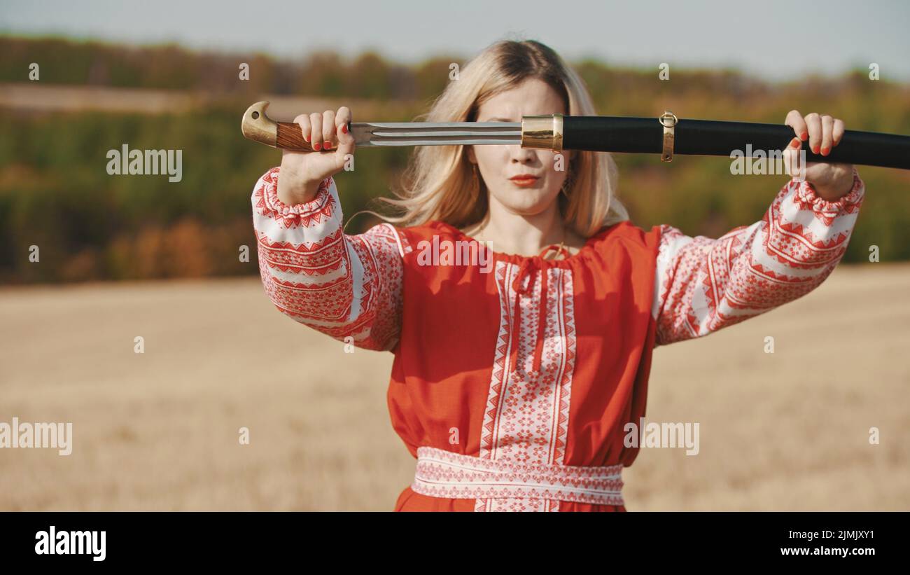 Feisty woman in red national dress pulls out a sword out of the sheath ...