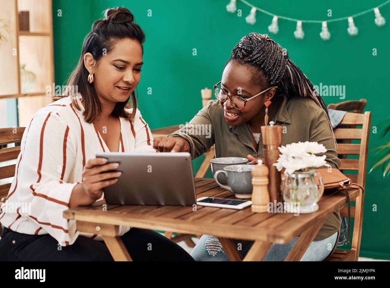 Who is that. two young women using a digital tablet together at a cafe ...