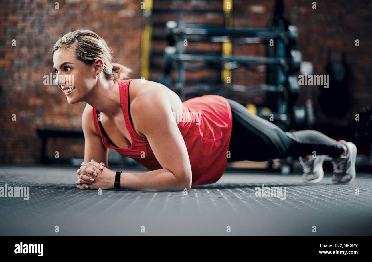 Hold the position. Full length shot of an attractive young female athlete planking in the gym ...