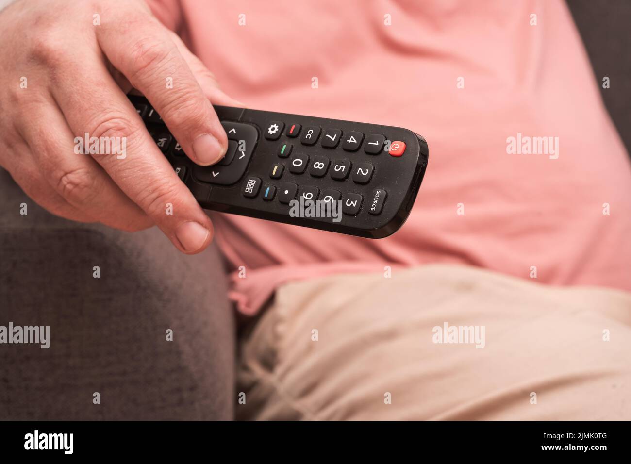 unrecognizable man sitting on a sofa with a remote control in his hand ...