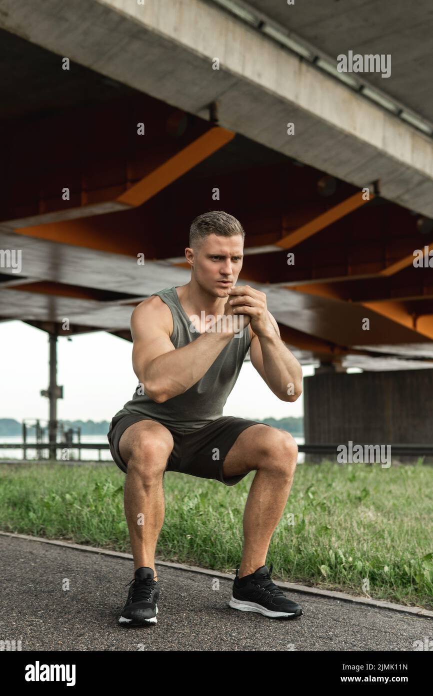 Muscular man is making squats under the bridge during his street ...