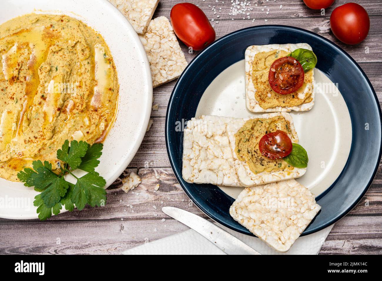 Square rice crackers with hummus and cherry tomatoes on a plate ...