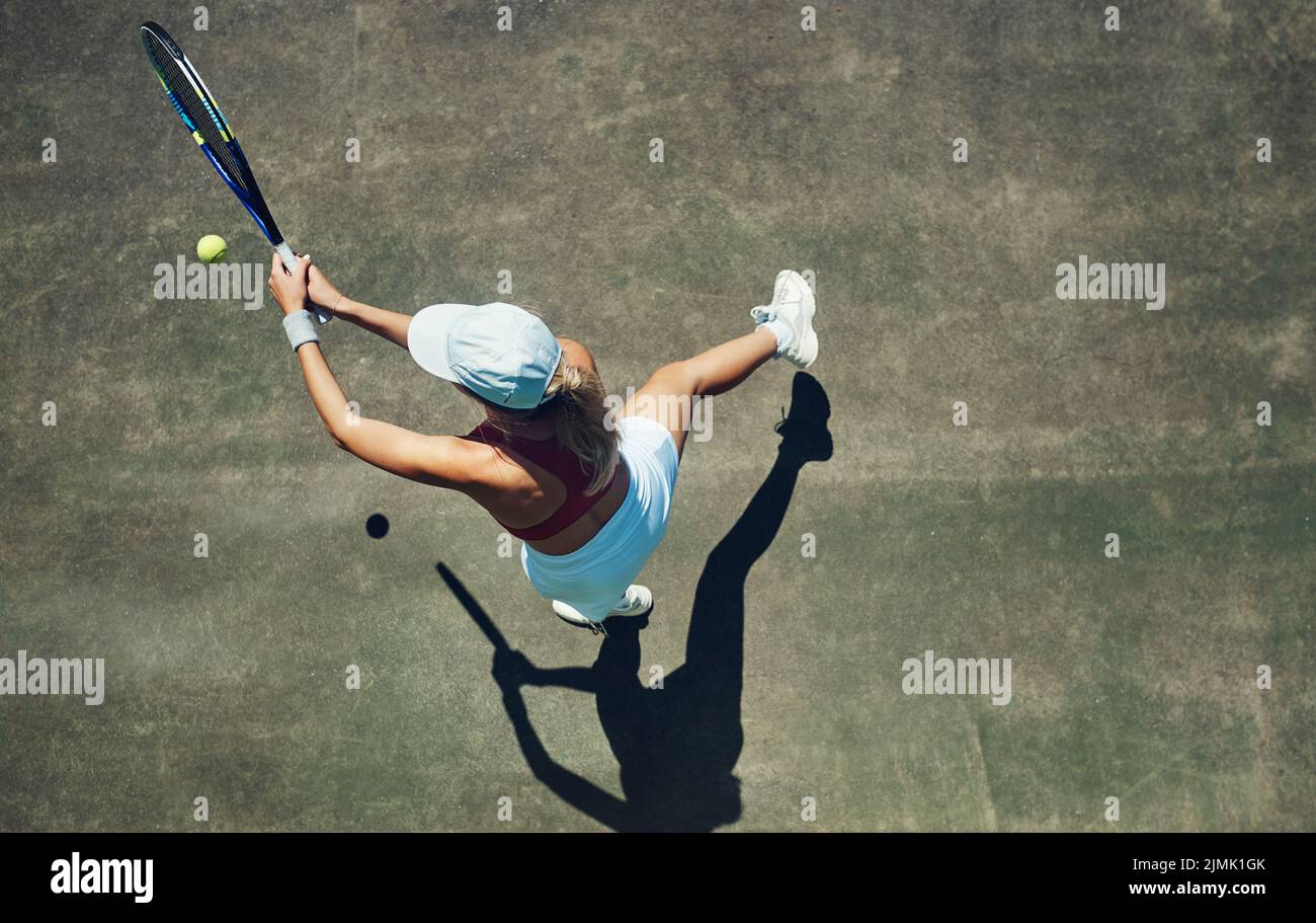 Keep swinging. High angle shot of a focused young woman playing tennis ...