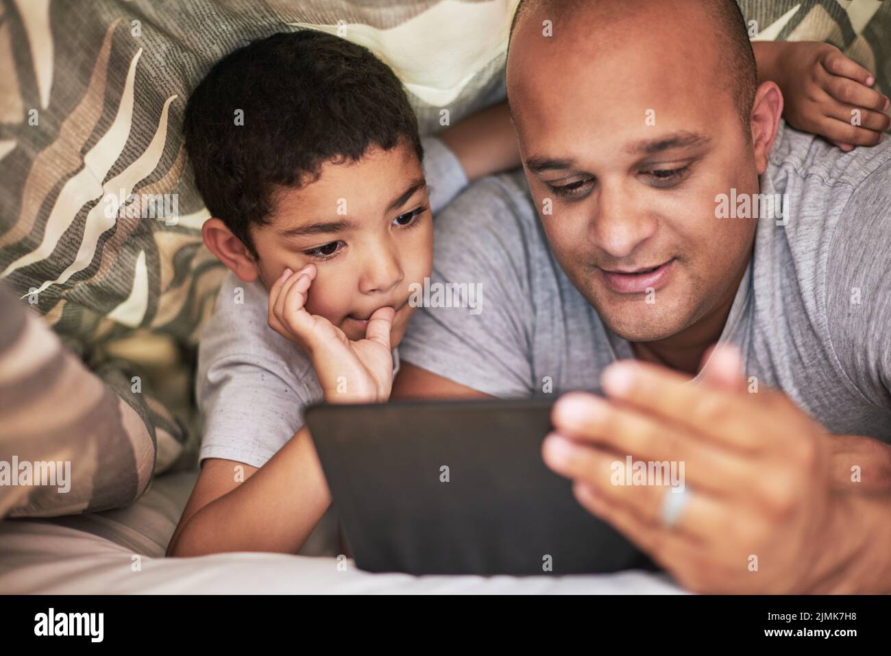 The show has their full attention. a cheerful young man and his son watching videos on a digital ...