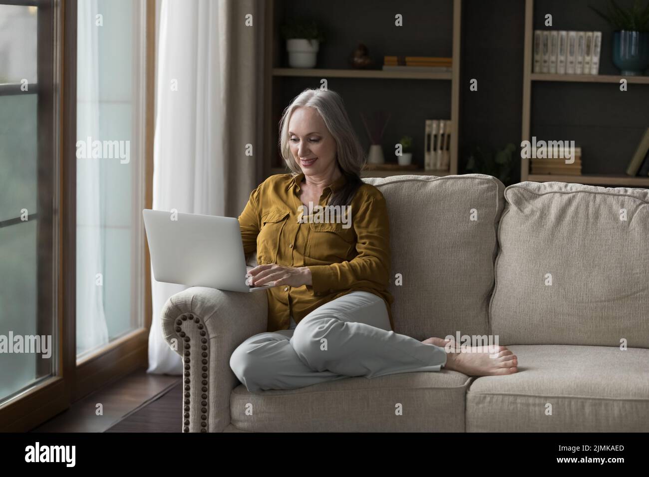 Happy elderly laptop user woman resting on soft couch Stock Photo - Alamy