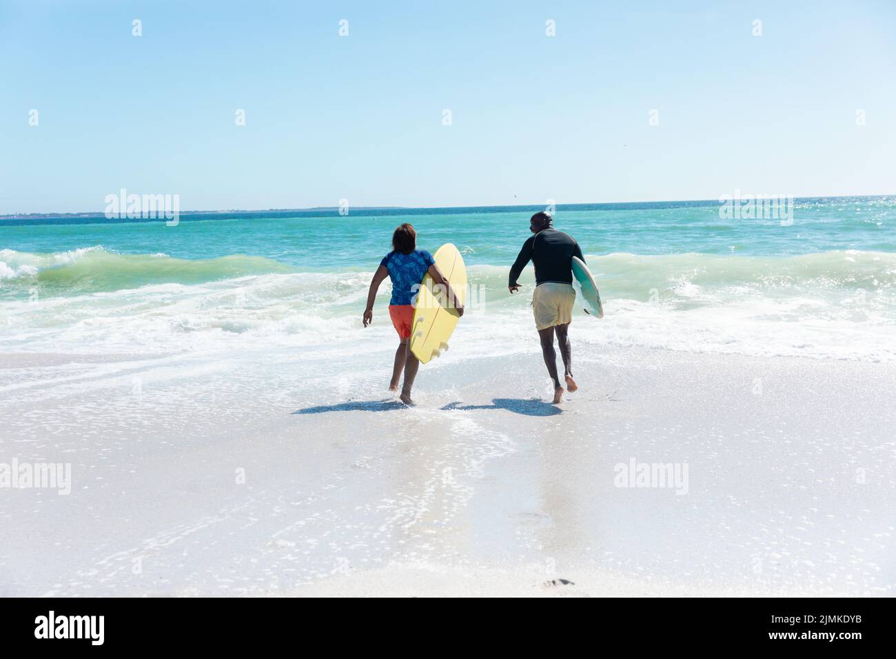 African american senior couple carrying surfboards running towards ...
