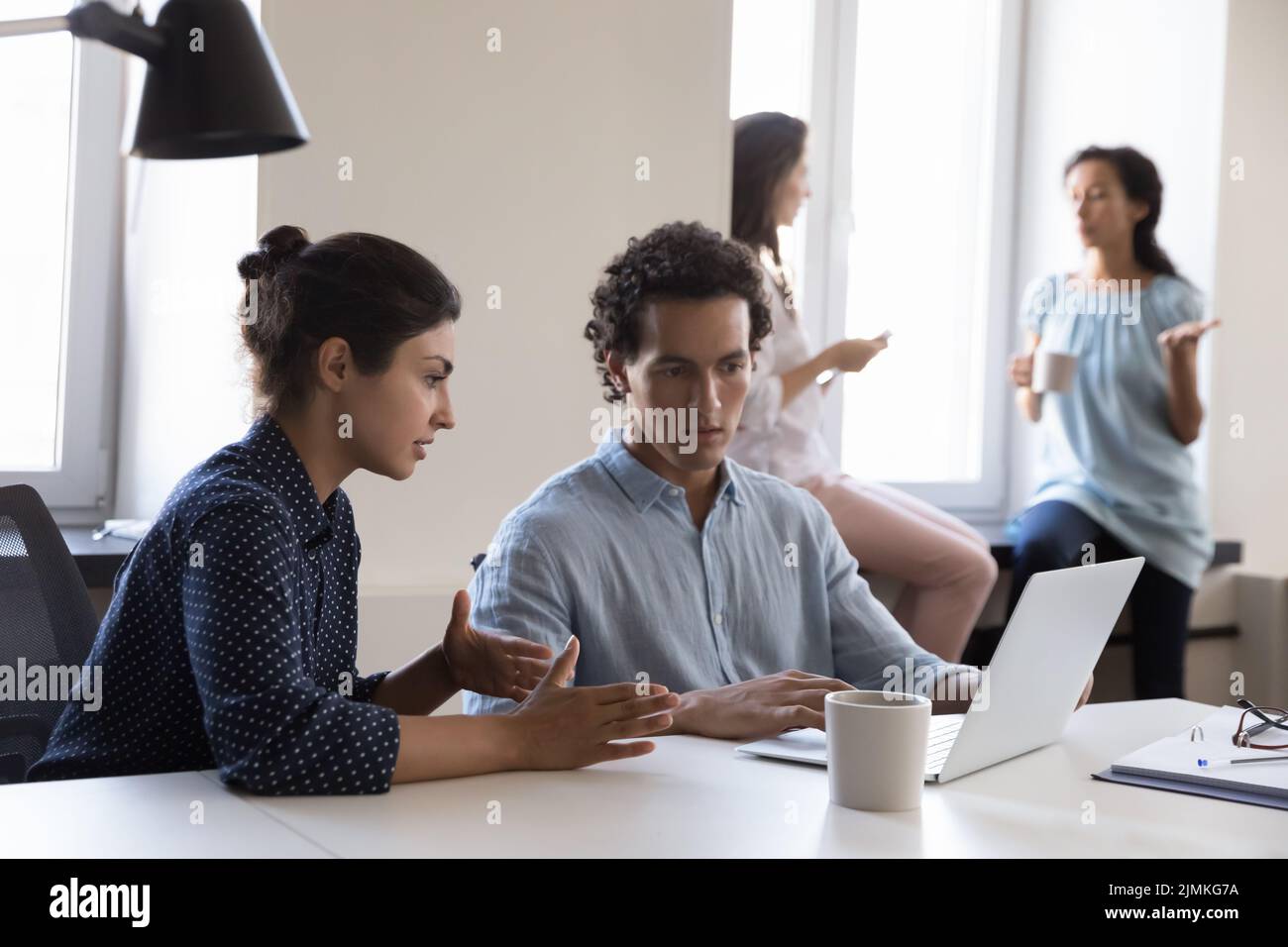 Multiracial colleagues talking sit at desk in office with laptop Stock ...