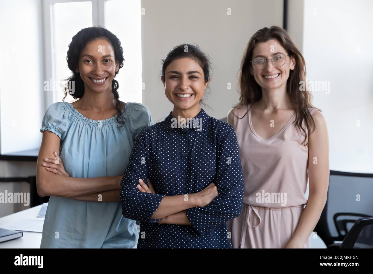 Three multiethnic businesswomen pose at workplace smile staring at ...