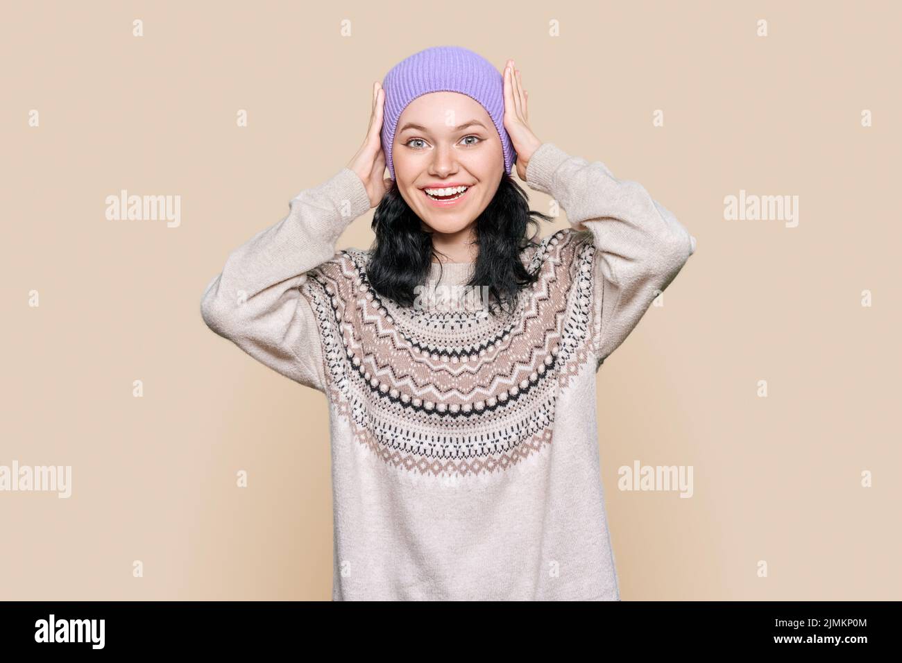 Happy emotional teenage female in sweater hat on light brown background ...