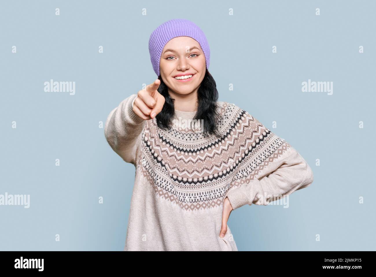 Teenage female in hat sweater pointing finger at you on gray background ...