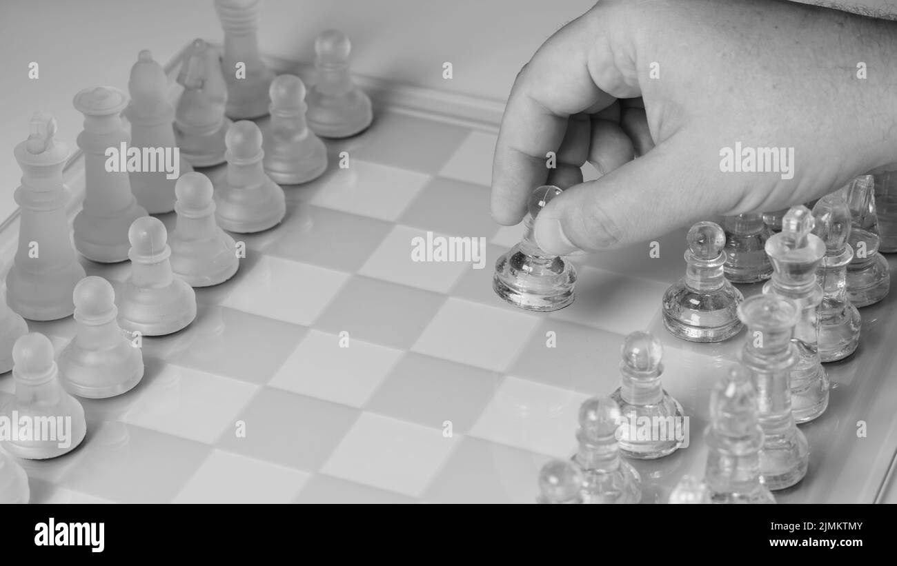 A chessboard with a hand starting to move a chess piece. Clear glass ...