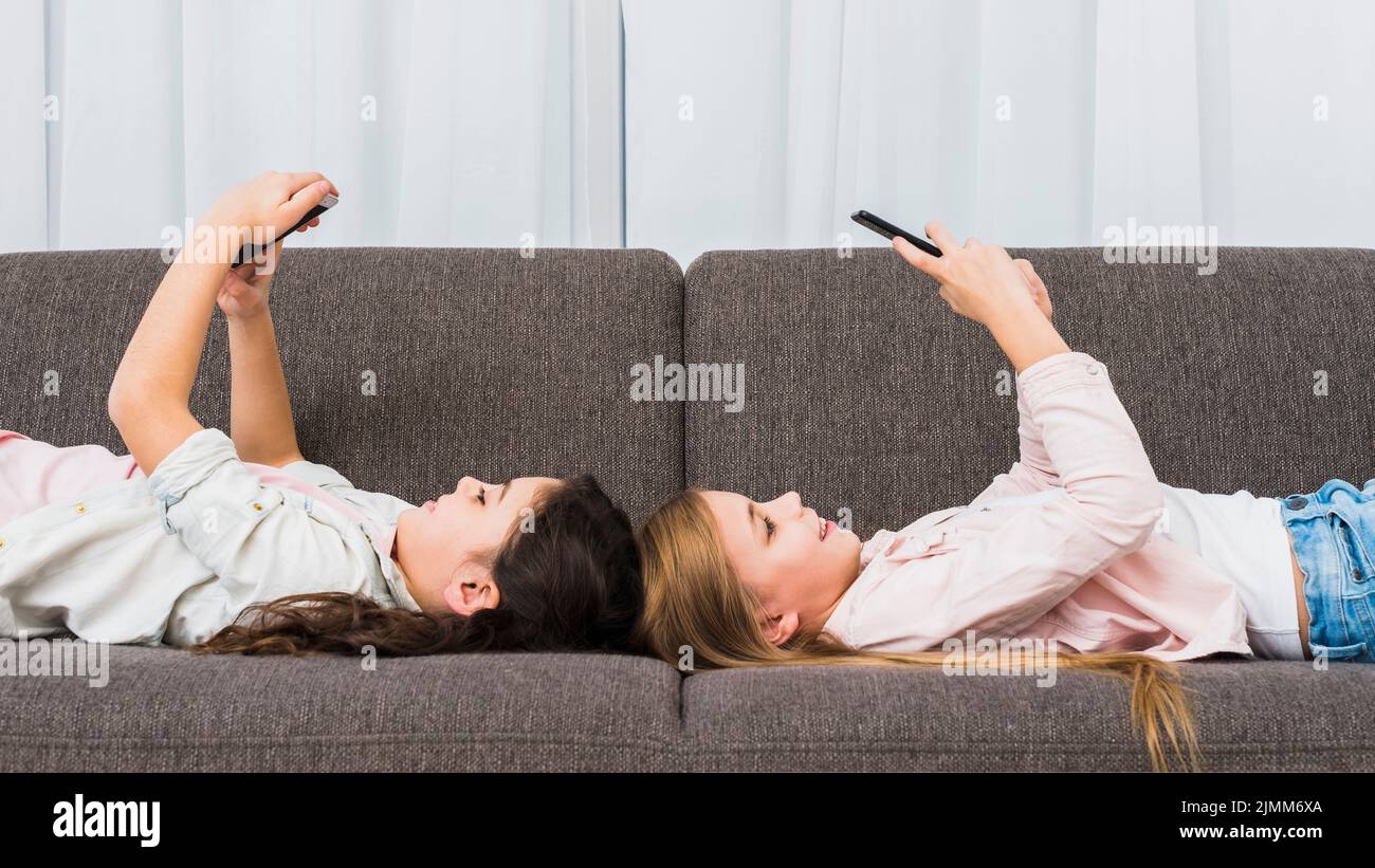 Happy female friends lying sofa using smart phone Stock Photo - Alamy