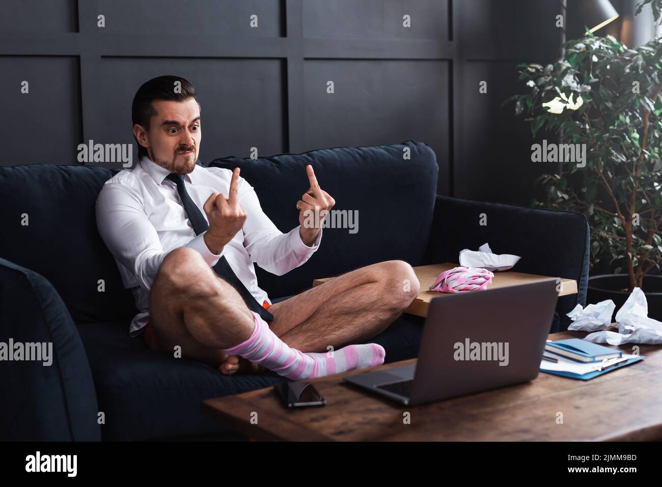 Angry businessman without pants showing rude gesture into the laptop's ...