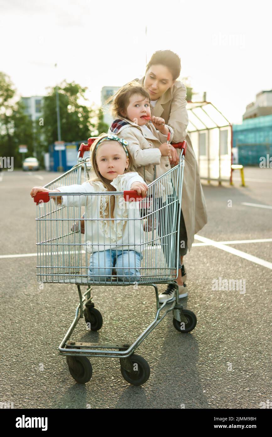 Happy mother and her daughters are having fun with a shopping cart on a ...