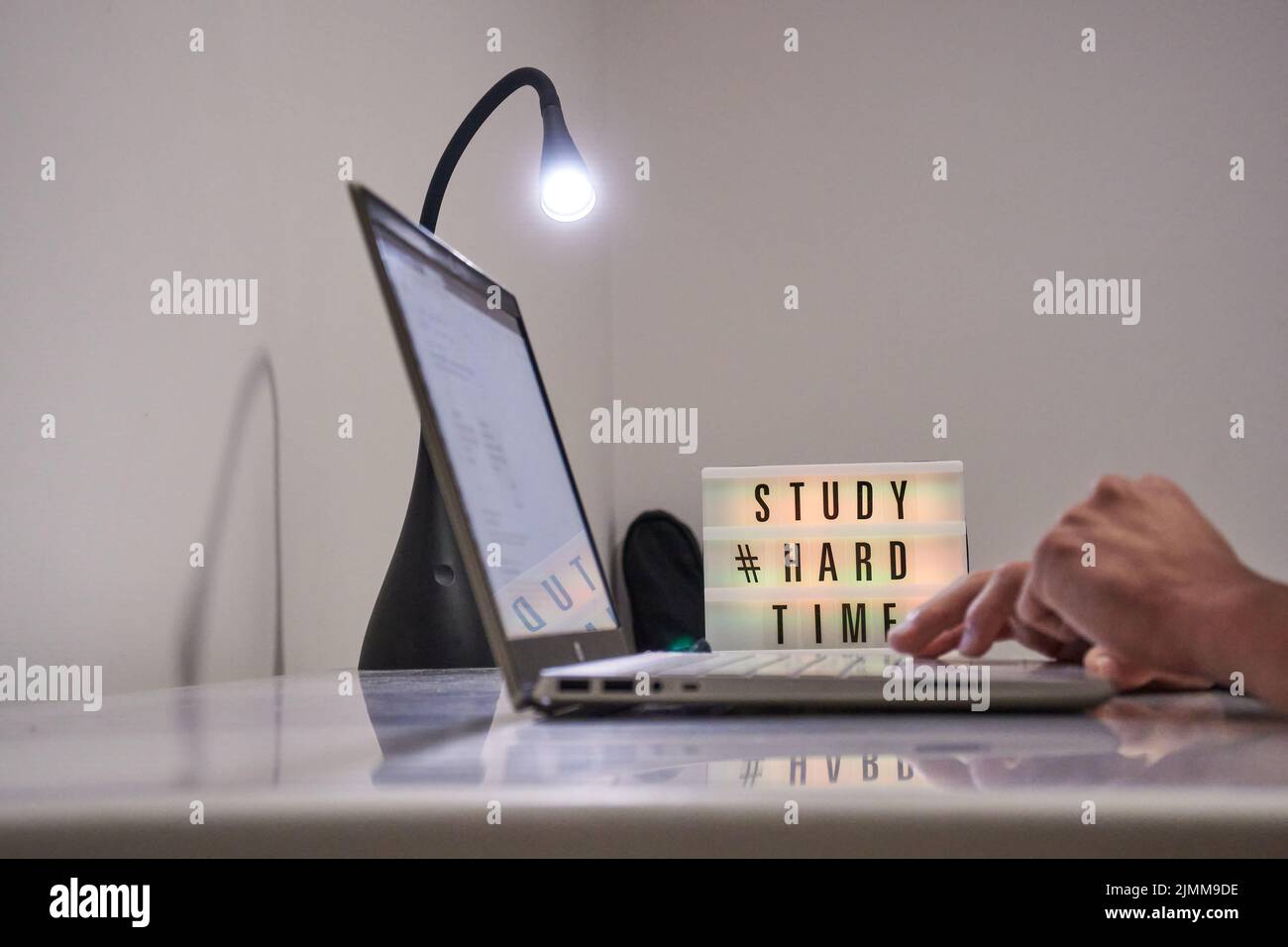A male working on the laptop with a lamp and a desk with text study ...