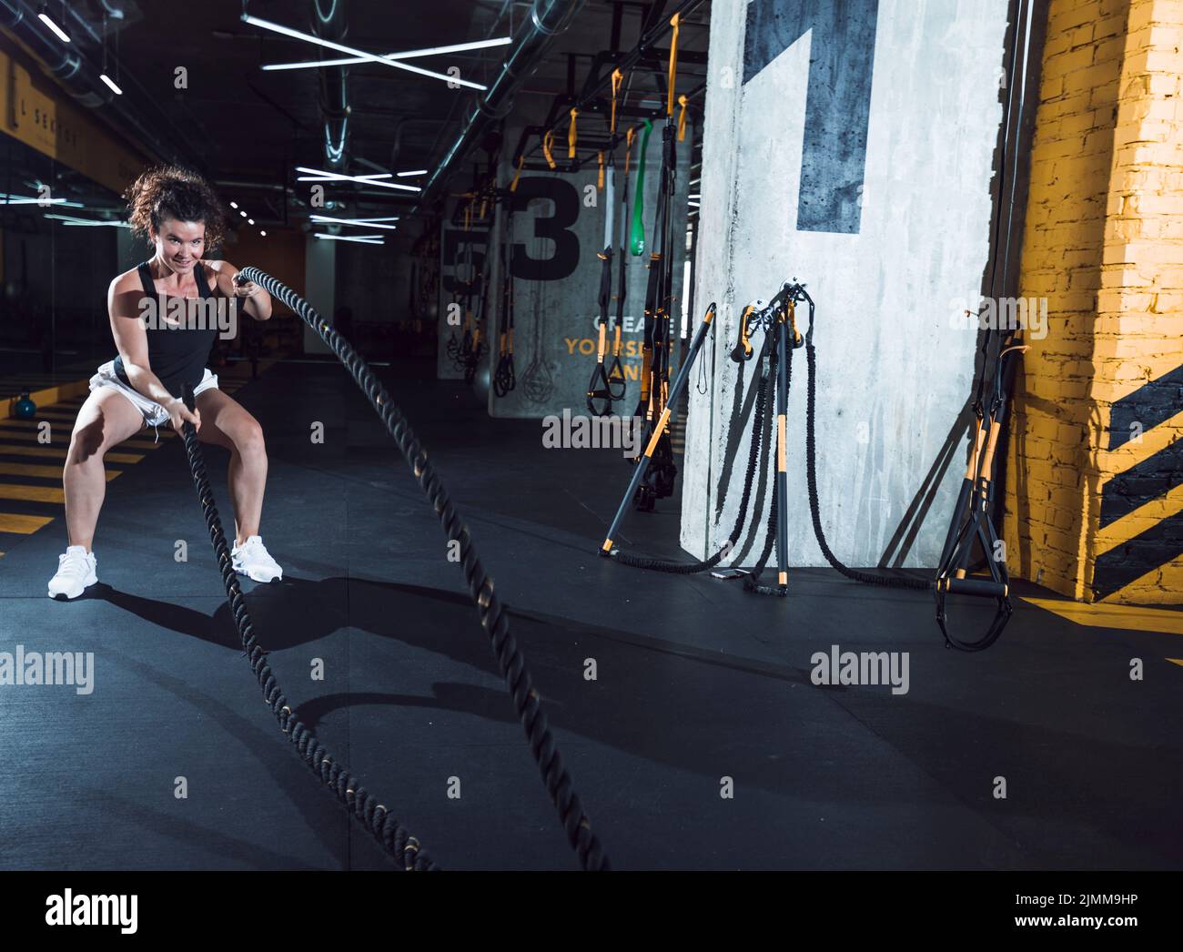 Smiling young woman exercising with battle ropes Stock Photo - Alamy