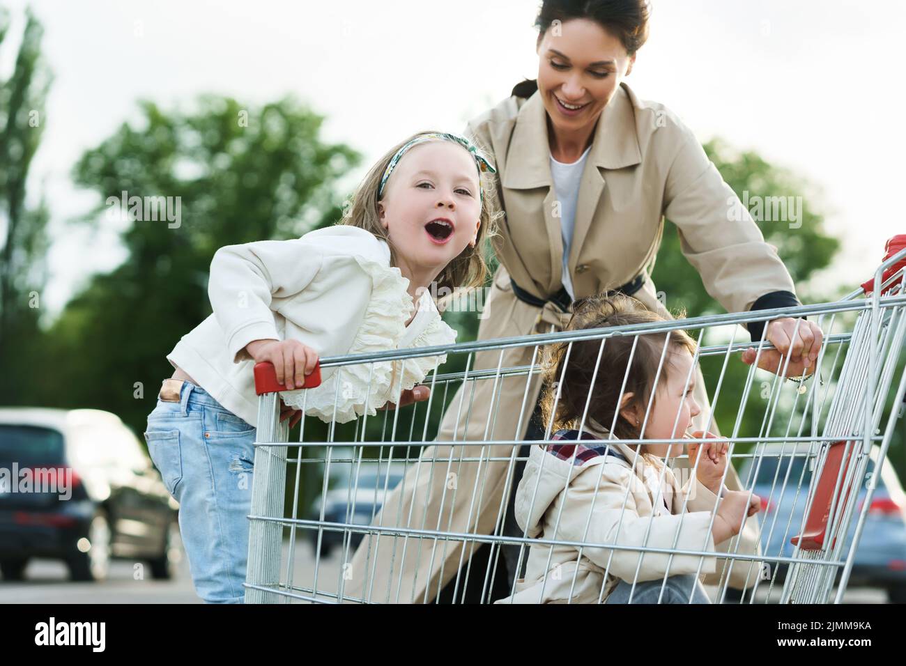 Happy mother and her daughters are having fun with a shopping cart on a ...