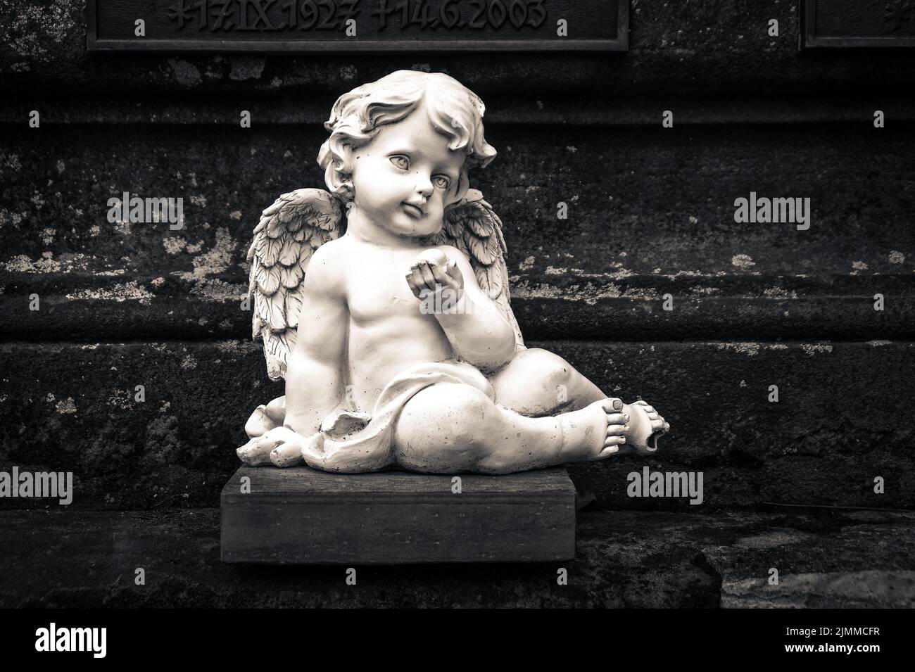 A sculpture of a baby angel leaning on a hard surface of a gravestone ...