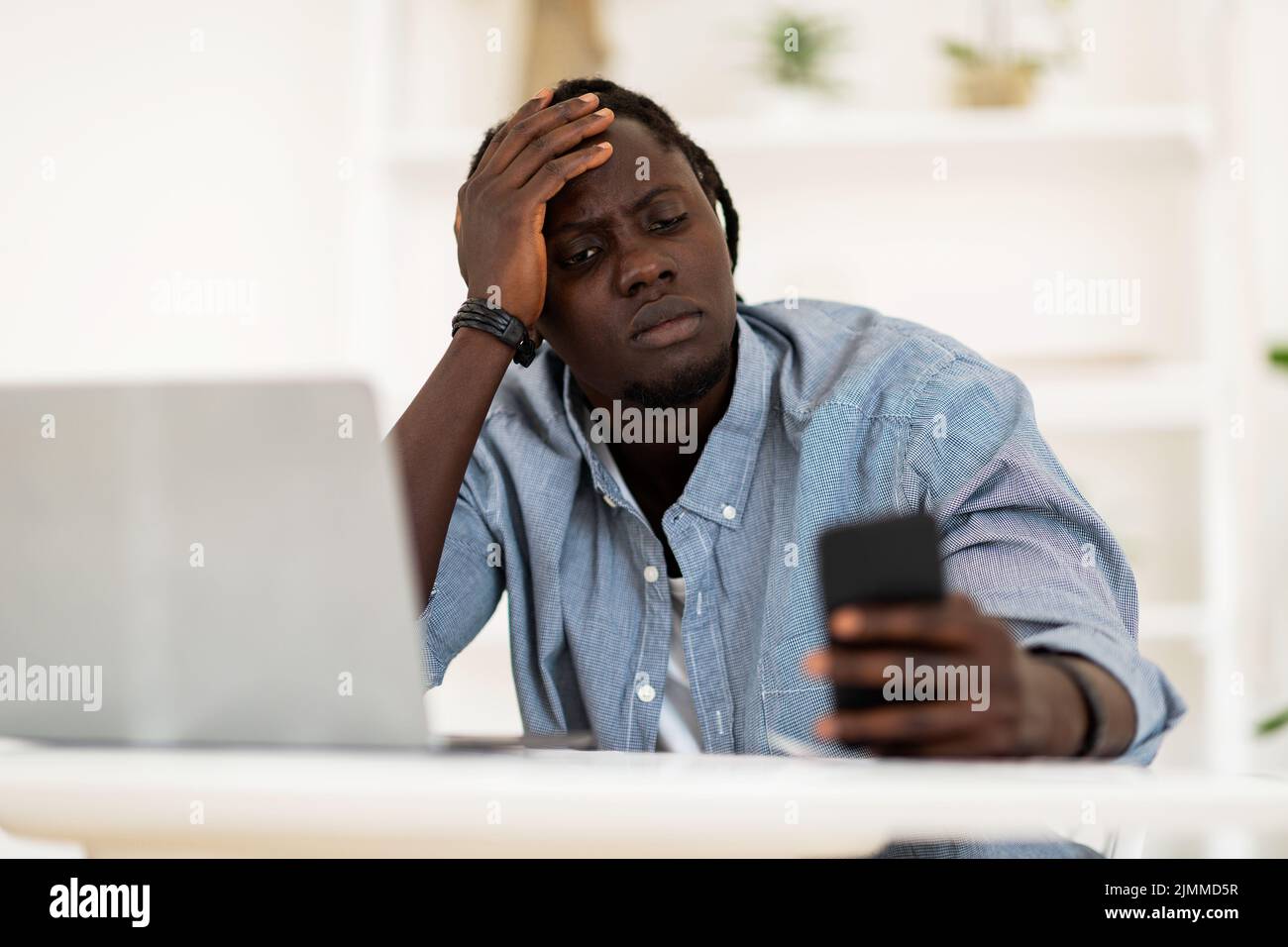 Bored Black Freelancer Guy Sitting At Desk And Holding Smartphone In ...