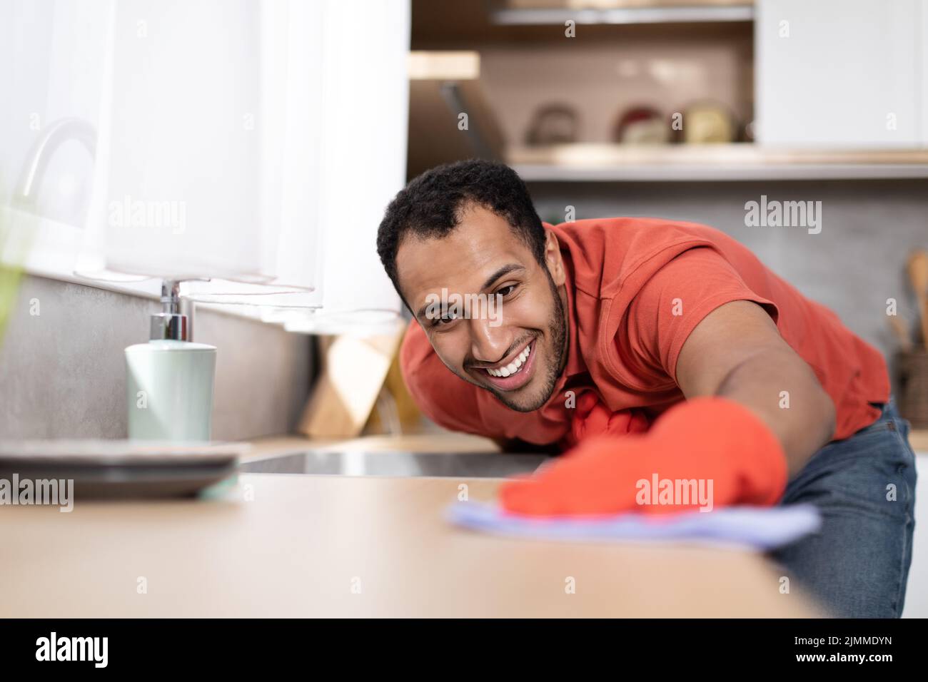 Happy handsome millennial african american guy in rubber gloves dusting ...