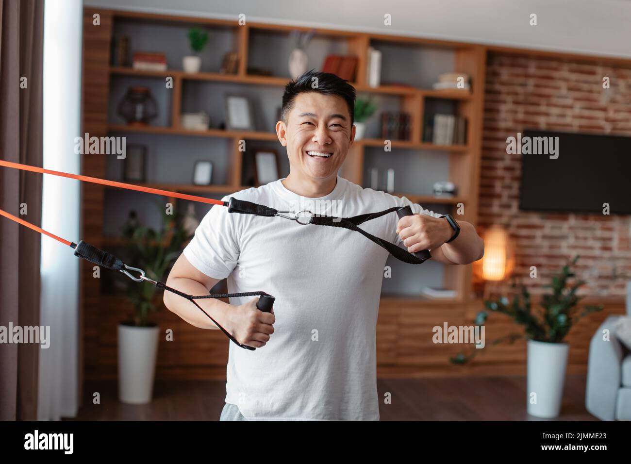Home fitness. Happy asian man exercising using resistance rubber band ...
