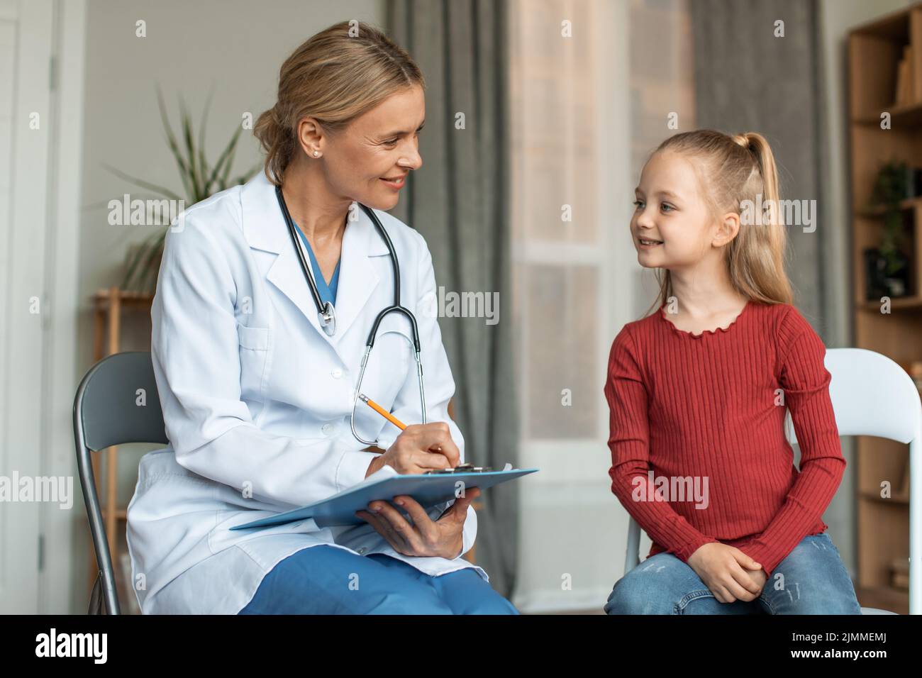 Pleasant female pediatrician talking to pretty schoolgirl patient and ...