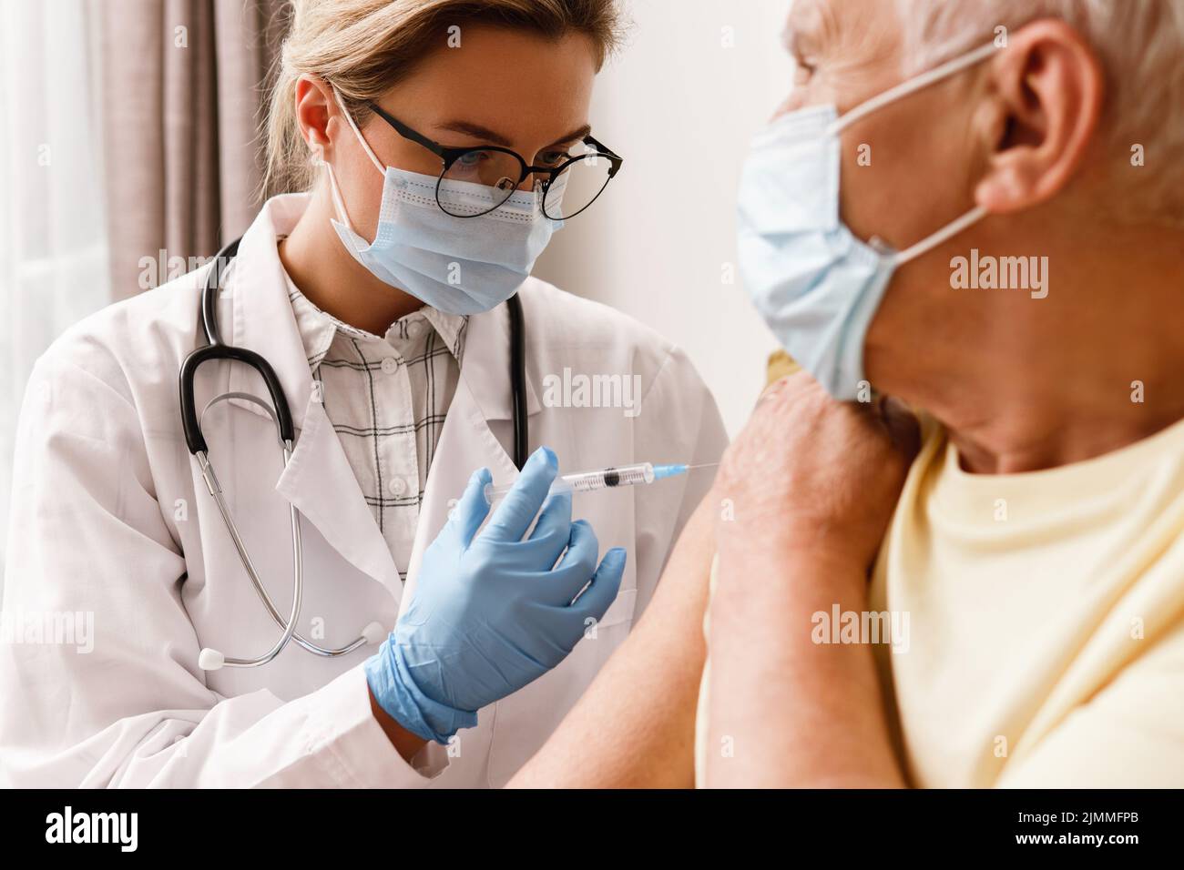 Doctor injecting vaccine to elderly man during home visit Stock Photo ...