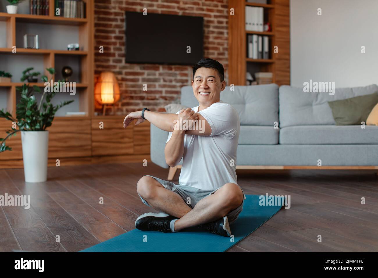 Sporty korean middle aged man stretching arm while exercising on yoga ...