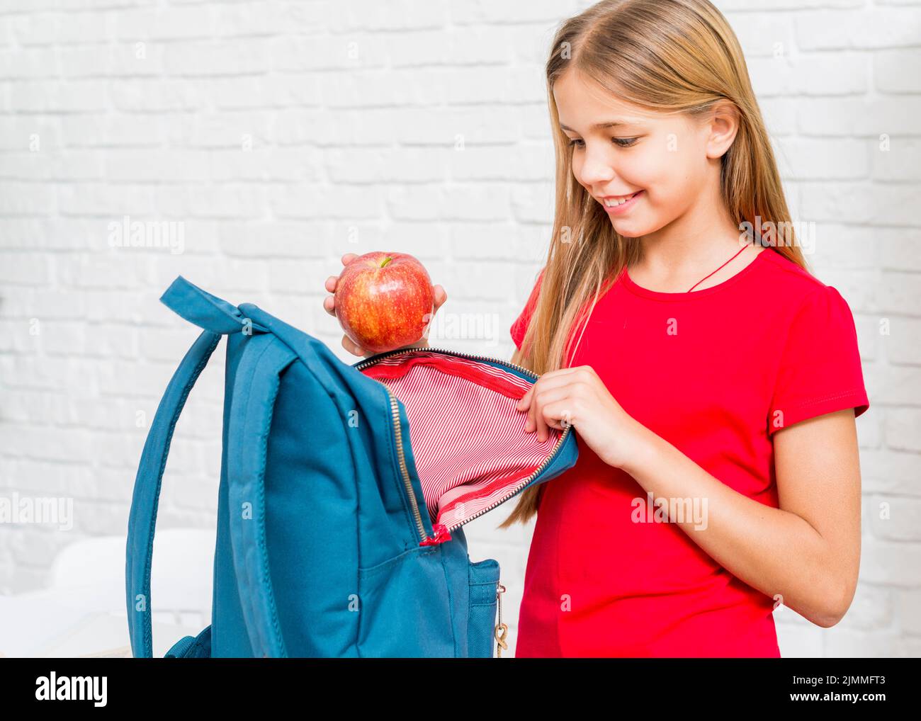 Happy girl putting apple backpack Stock Photo - Alamy