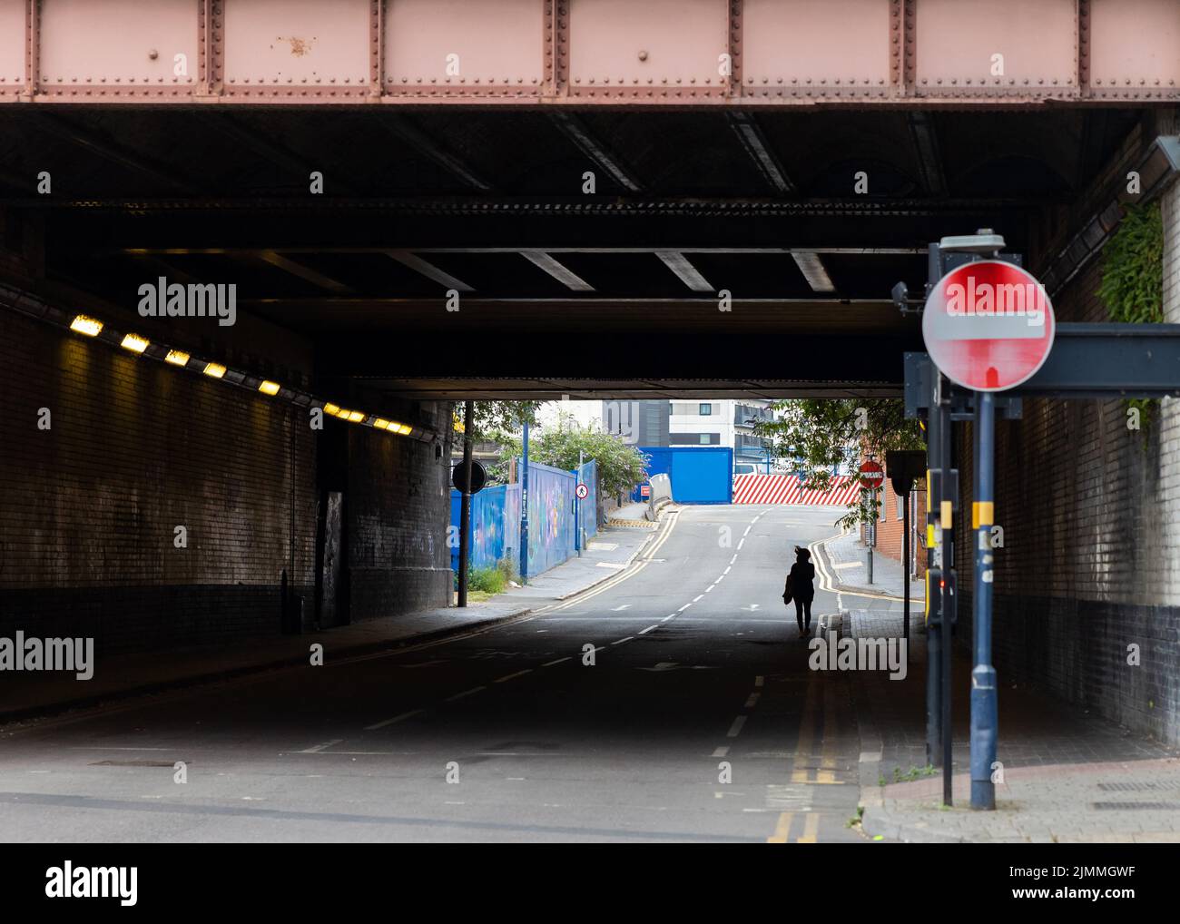 Lone female walking under bridge on deserted street in rundown area of ...