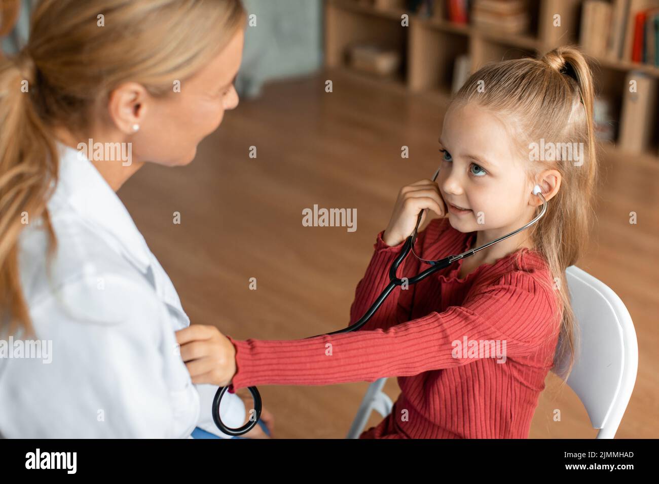 Pretty little girl visiting pediatrician and playing with female doctor, listening doc's heart ...