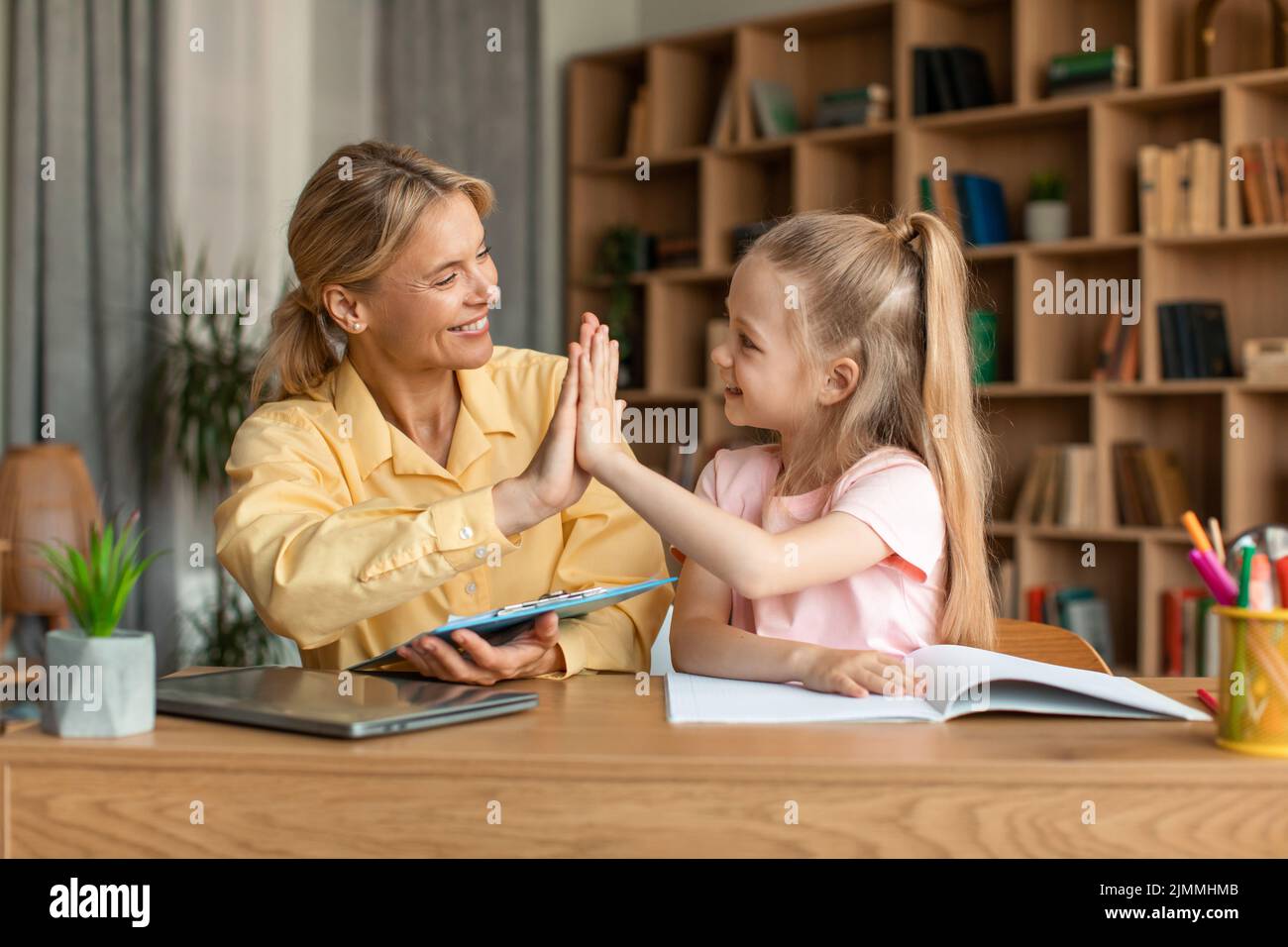 Well done. Excited teacher giving high five to little girl, greet ...