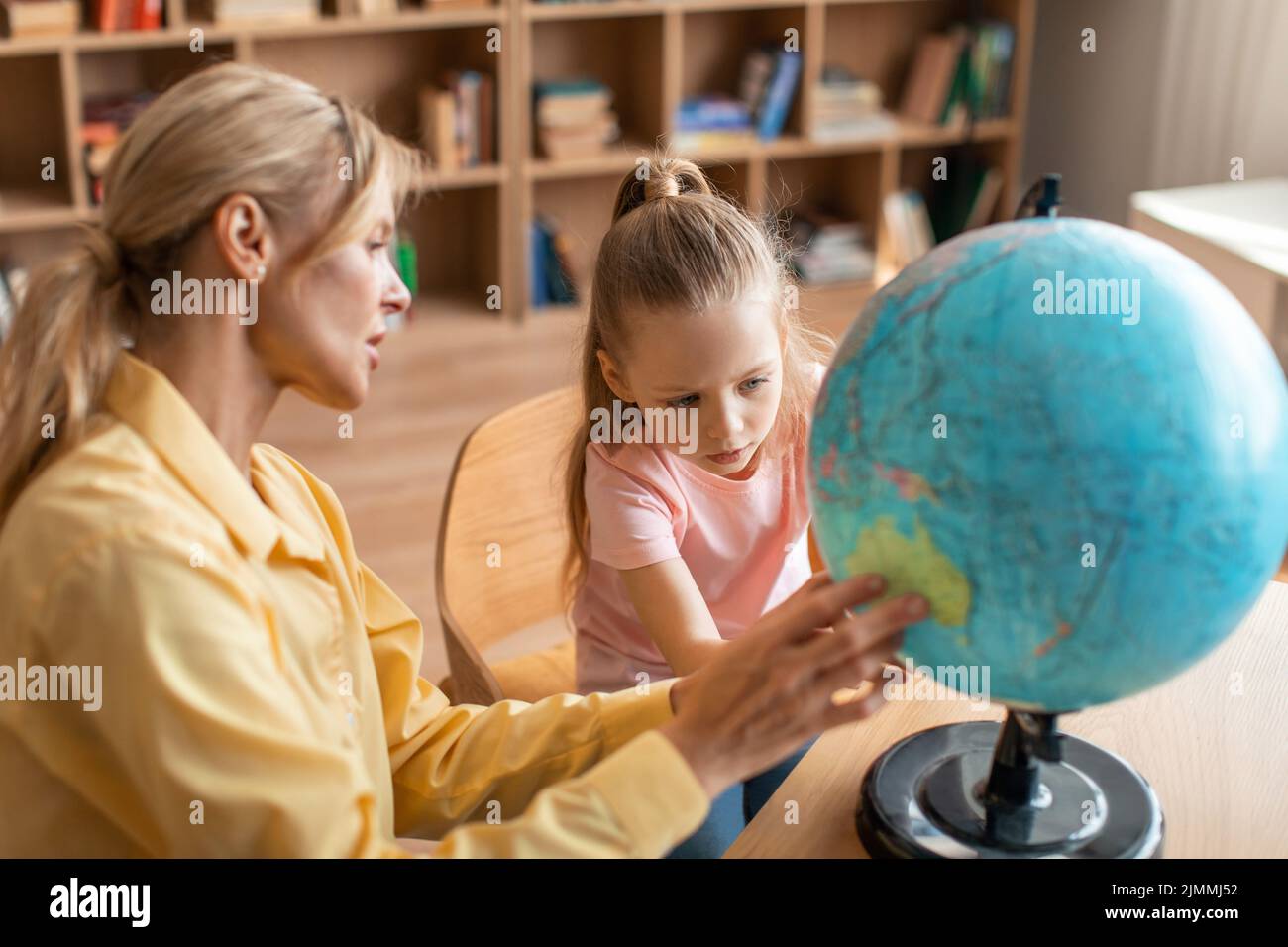 Female private preschool teacher teaching smart girl about globe ...