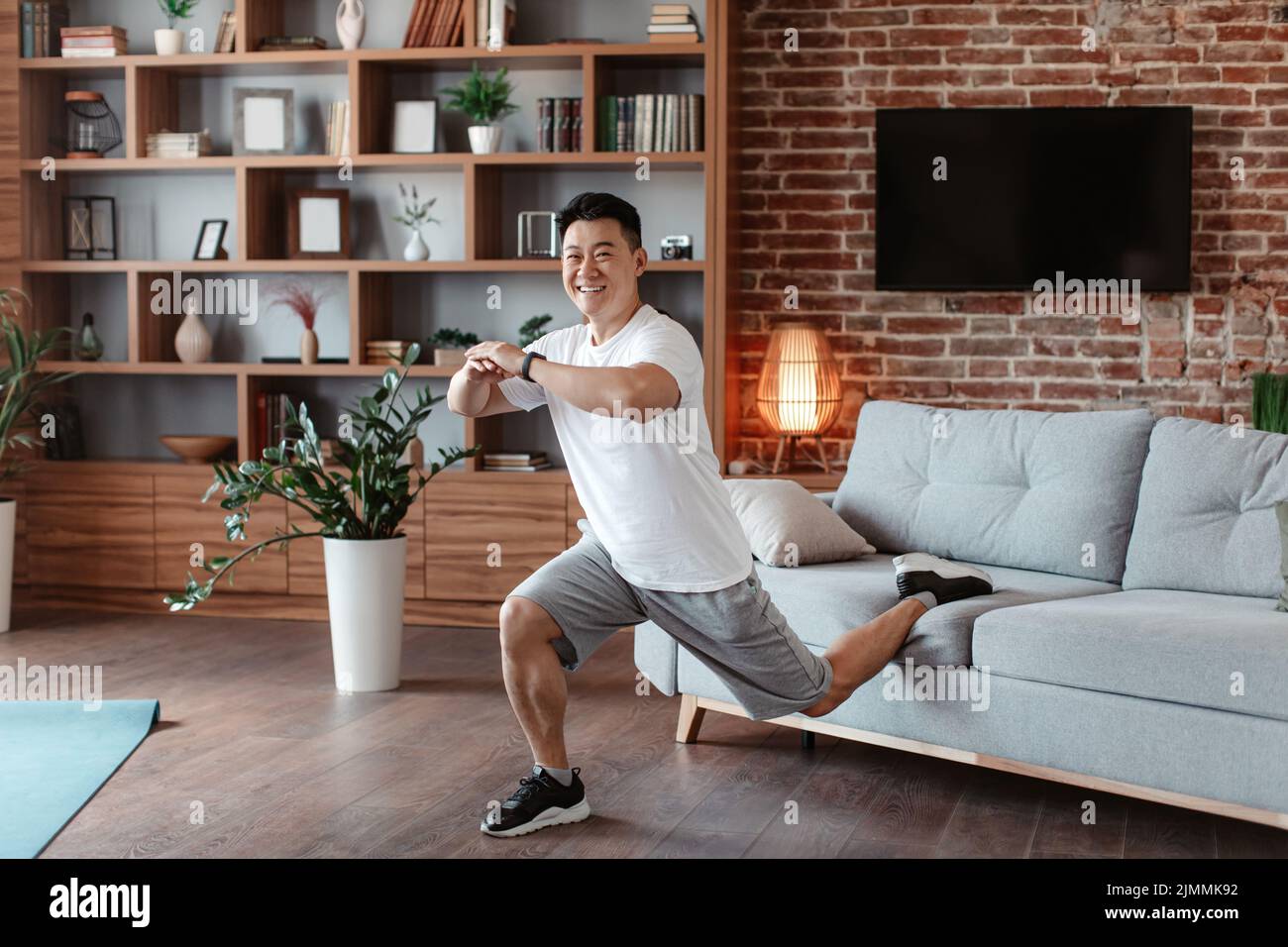 Home workout concept. Excited asian mature man doing single leg split ...