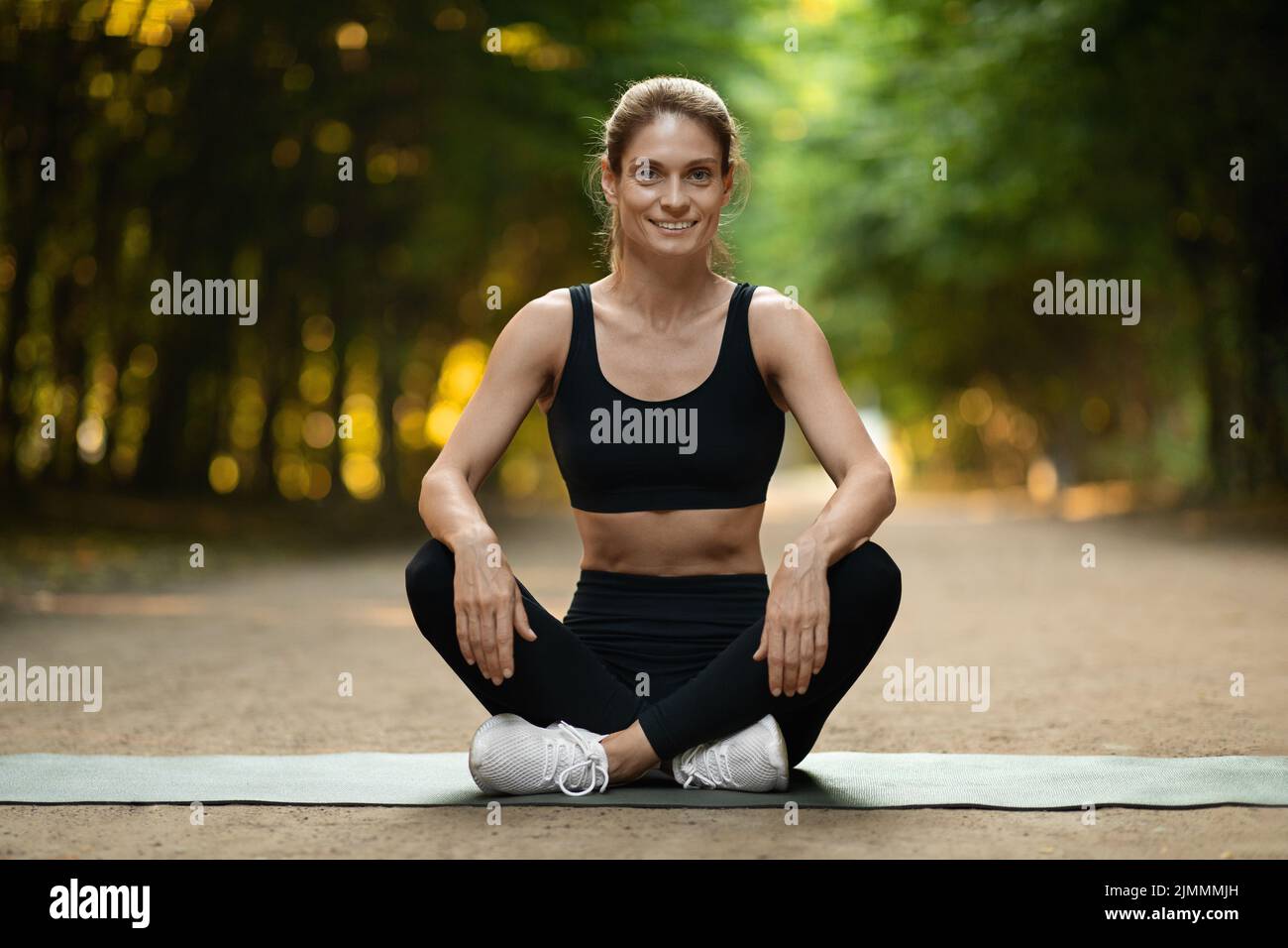 Happy woman in sportswear sitting on fitness mat Stock Photo - Alamy
