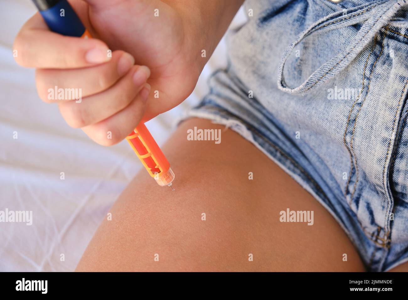 Close-up of a girl using an insulin pen to inject insulin into her leg ...
