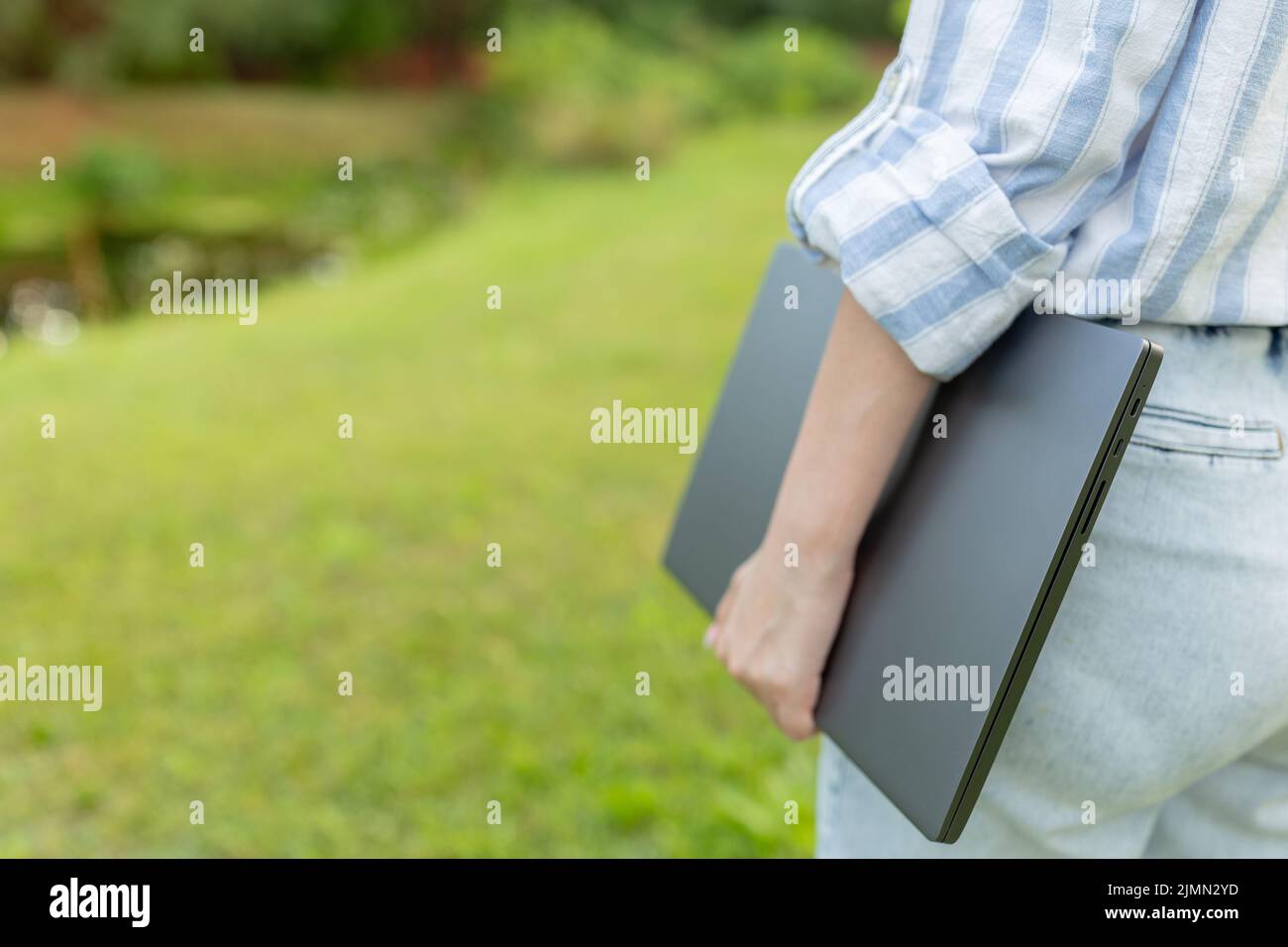 Back view of a woman who is standing with a closed laptop. Rear view ...