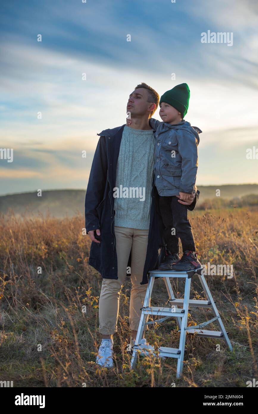 Caucasian father stands with his son on the hilltop and looking far ...