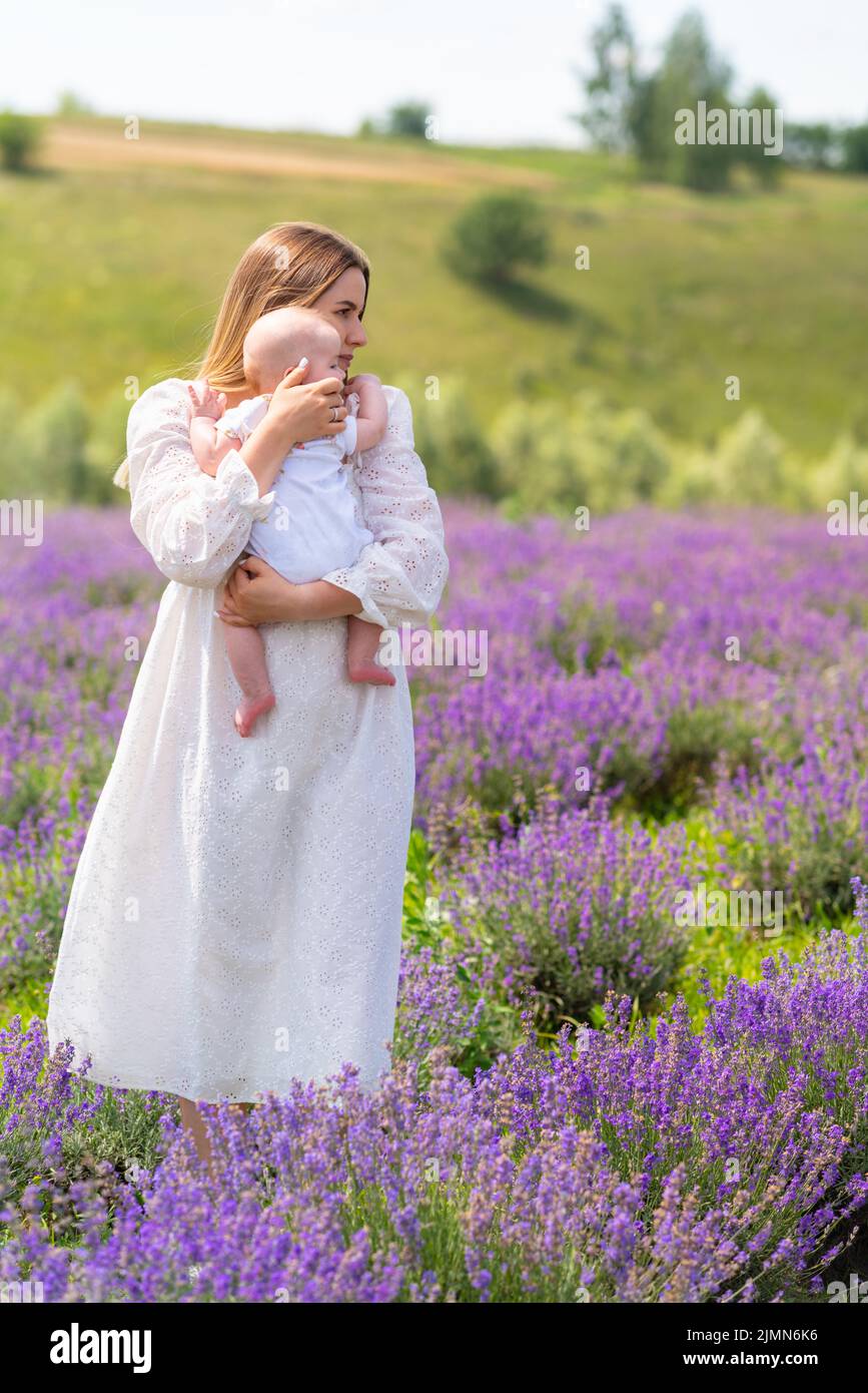 Young mother cradling her little baby in her arms as she poses outdoors ...