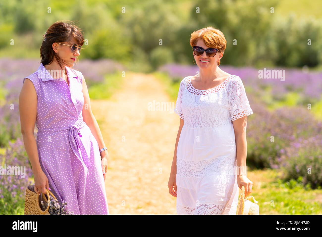 Two lady friends posing standing in a field of lavender in stylish ...