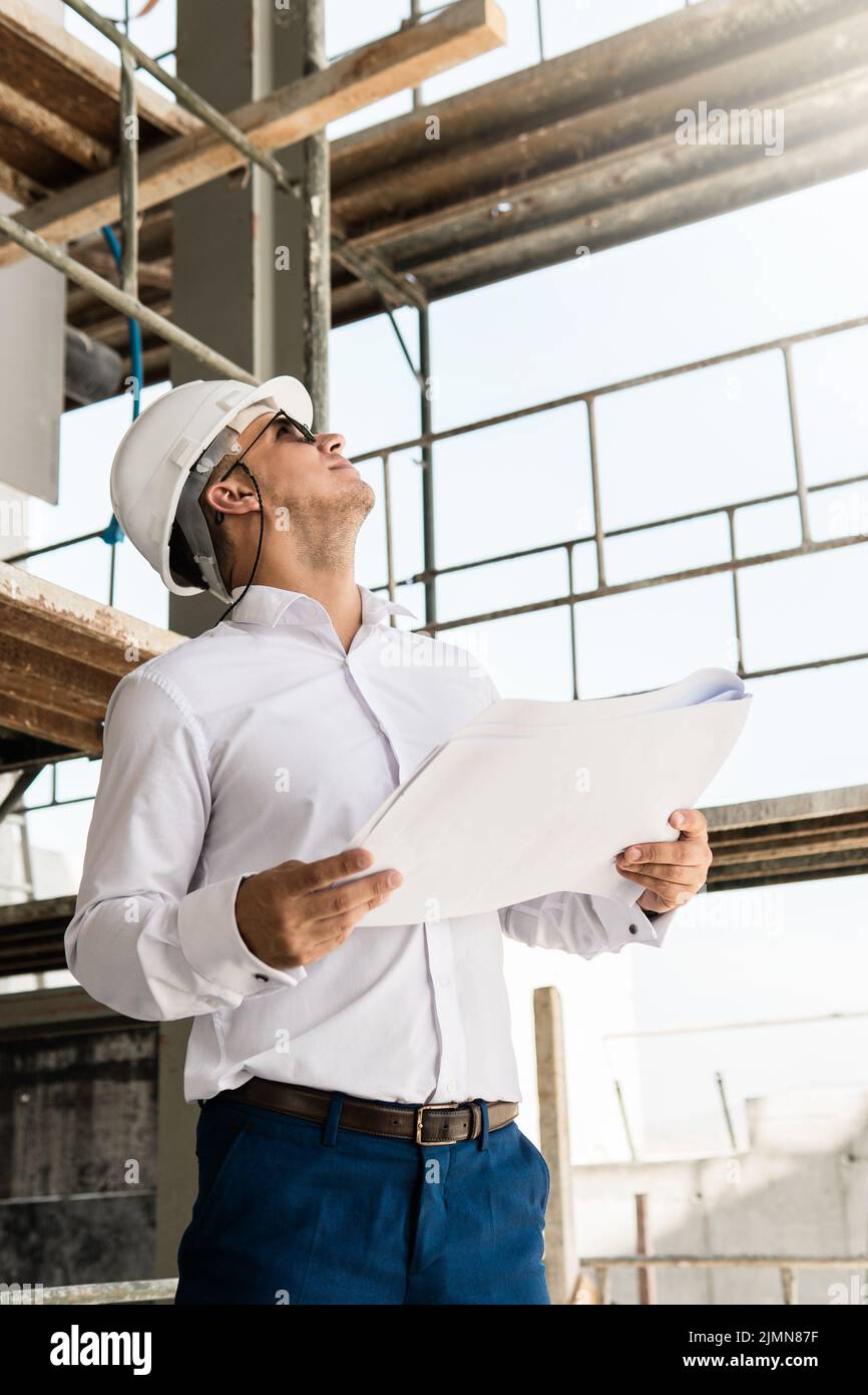 Man architect or businessman wearing hard hat and holding blueprints on ...