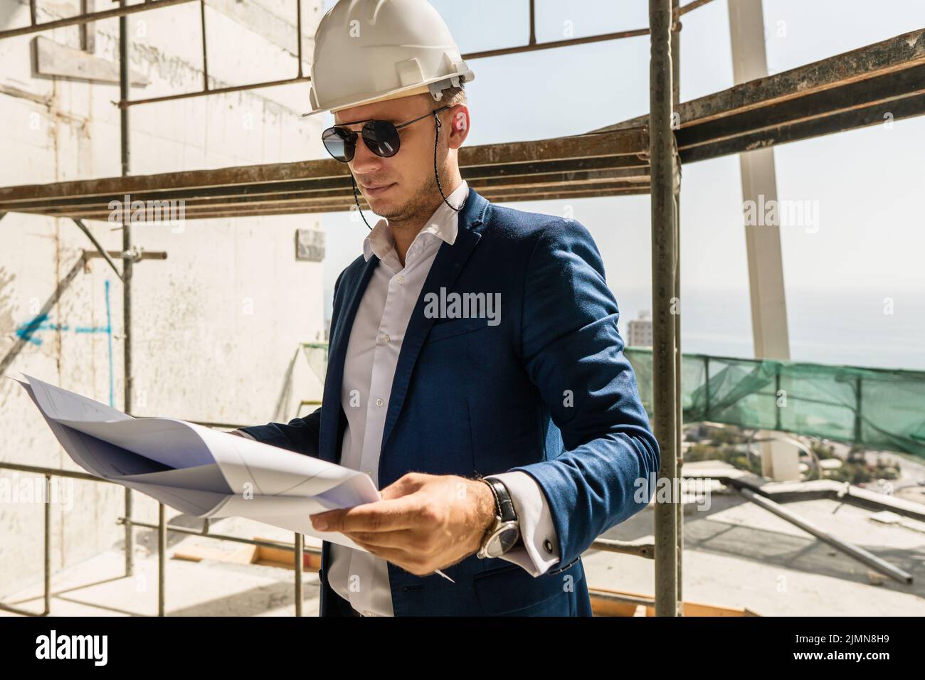Architect wearing formal suit and hard hatholding a blueprints on a ...