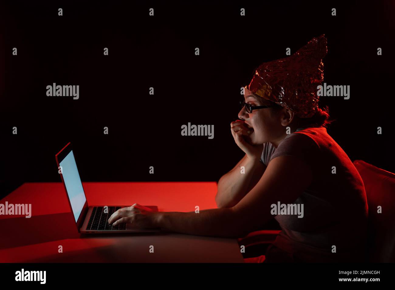 Paranoid caucasian woman typing on a computer wearing a tinfoil cap ...