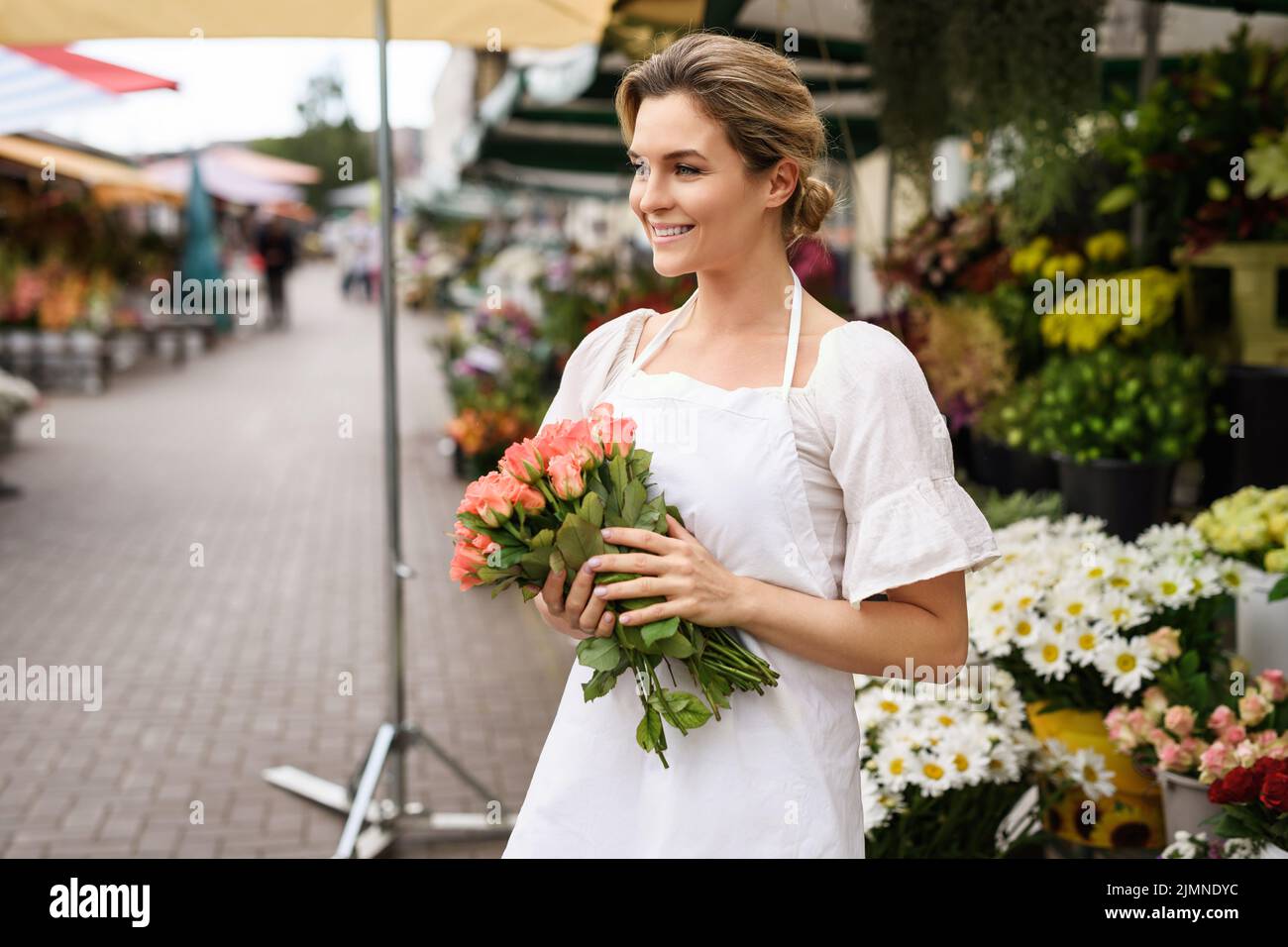 Woman florist with a heap of rose flowers in her little flower shop ...