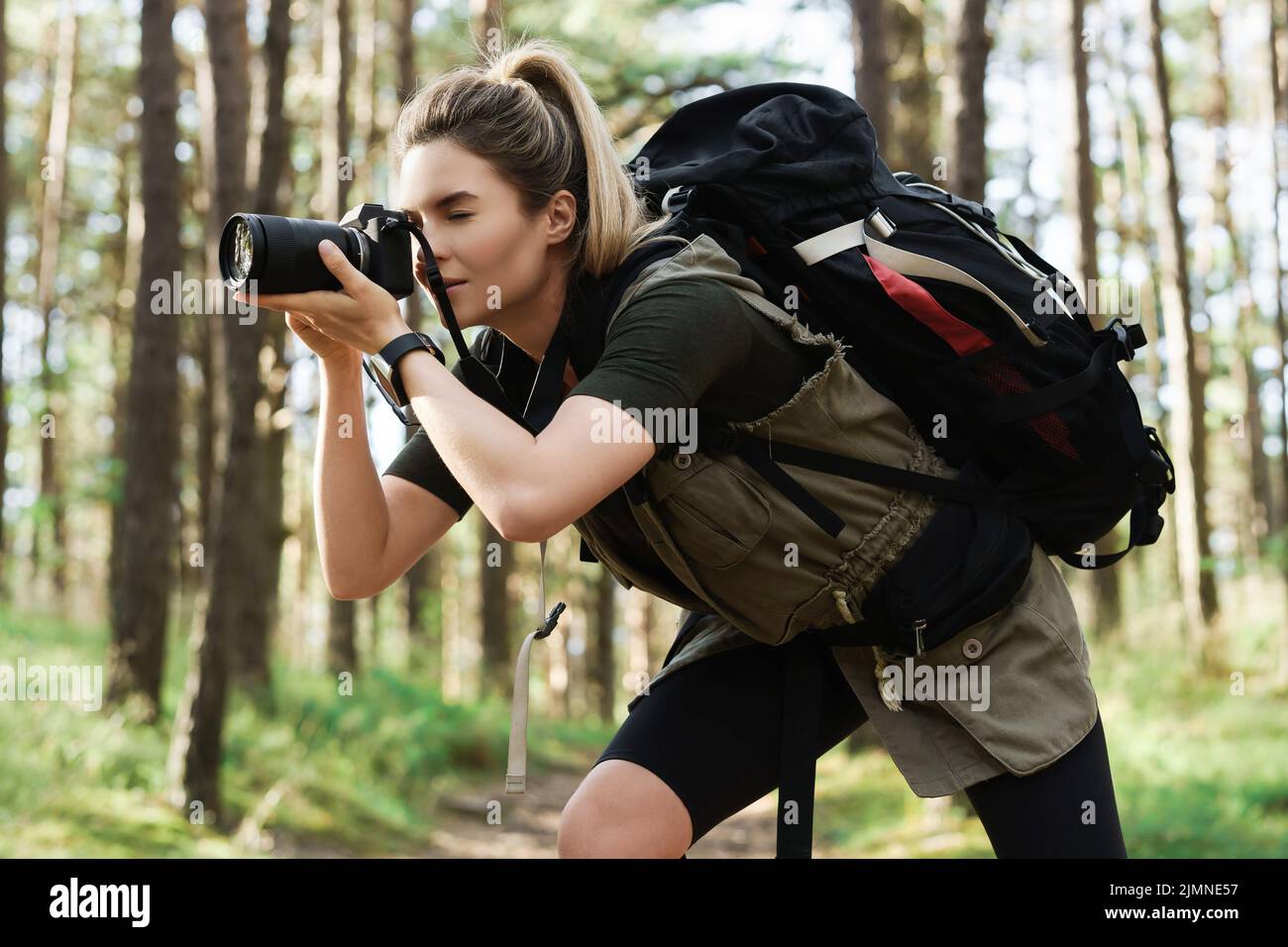 Hiker taking photos using modern mirrorless camera in green forest ...