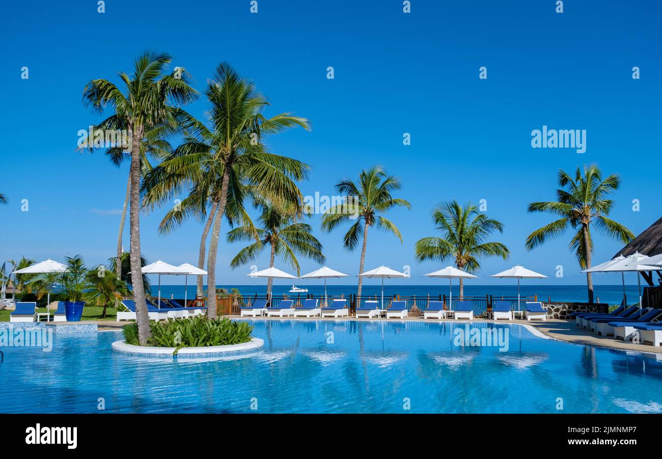 Beautiful tropical beach front hotel resort with swimming pool, sun-loungers and palm trees ...