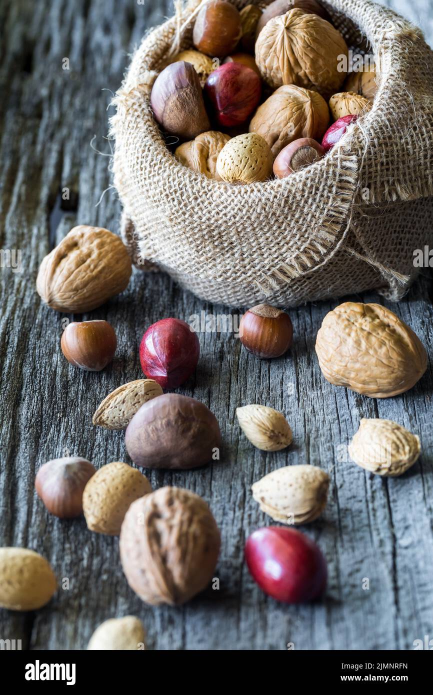 A burlap sack filled with mixed whole nuts with several spilled out in ...