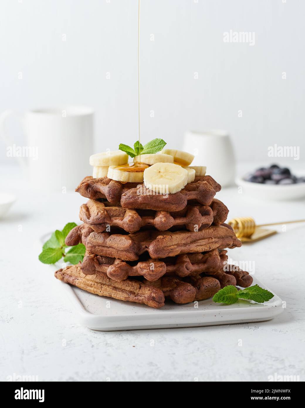 Chocolate banana waffles with maple syrup on white table, side view ...