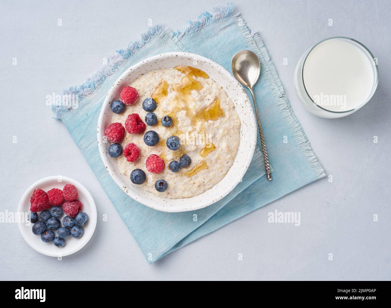Oatmeal with berries, chia, maple syrup and glass of milk on blue light ...